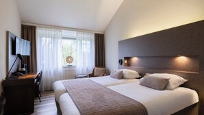 Quarto de hotel com duas camas, uma mesa de trabalho com cadeira, televisão e janela com cortinas.