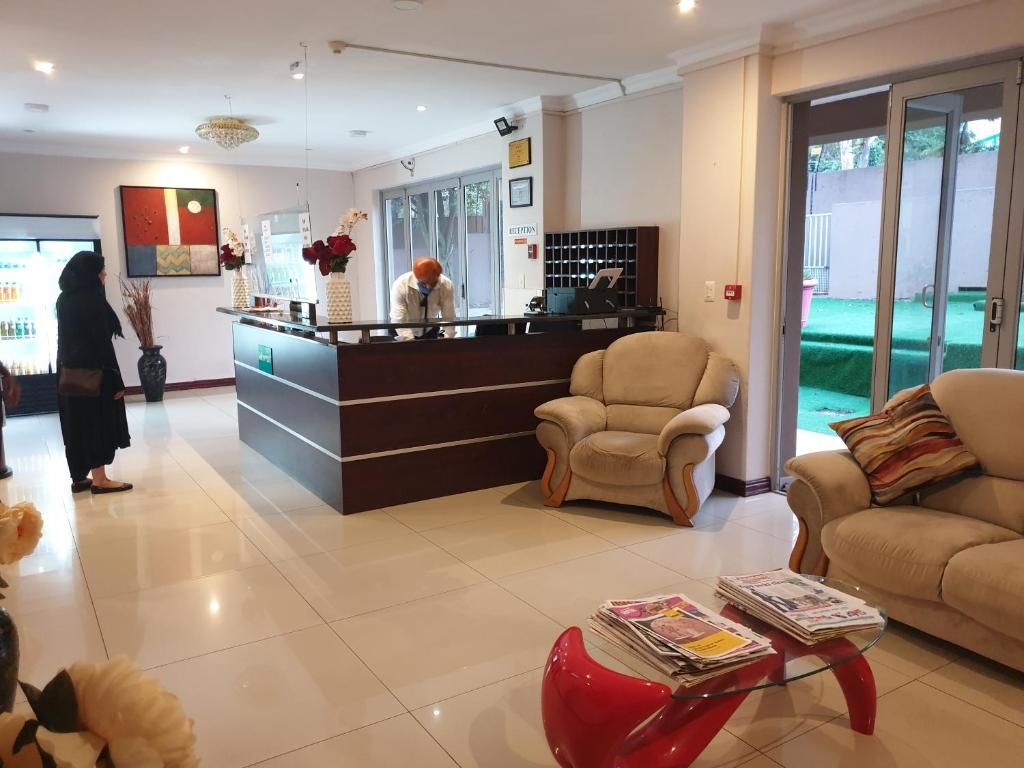 Um saguão de hotel com balcão de recepção, área de estar e uma mesa de centro de vidro com revistas.