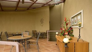 Quarto com um balcão de recepção de madeira, uma mesa redonda com cadeiras e piso de azulejos.