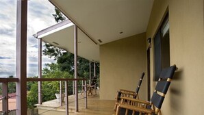 Um deck de madeira com duas cadeiras e uma mesa, com vista para um jardim e um edifício.