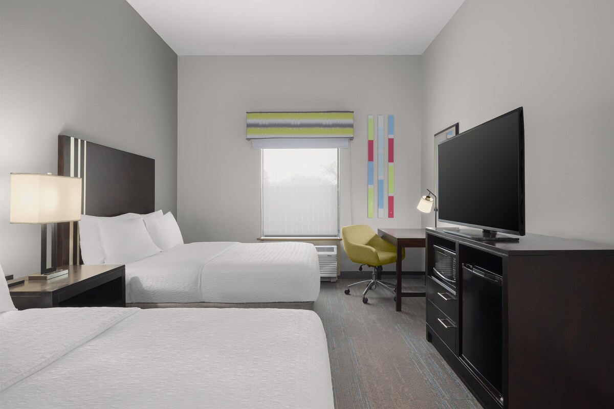 Quarto de hotel com duas camas, uma escrivaninha, uma televisão e uma cadeira.