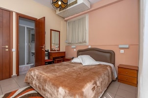 Um quarto com uma cama grande, uma escrivaninha, uma cadeira, um guarda-roupa e uma janela com cortinas.