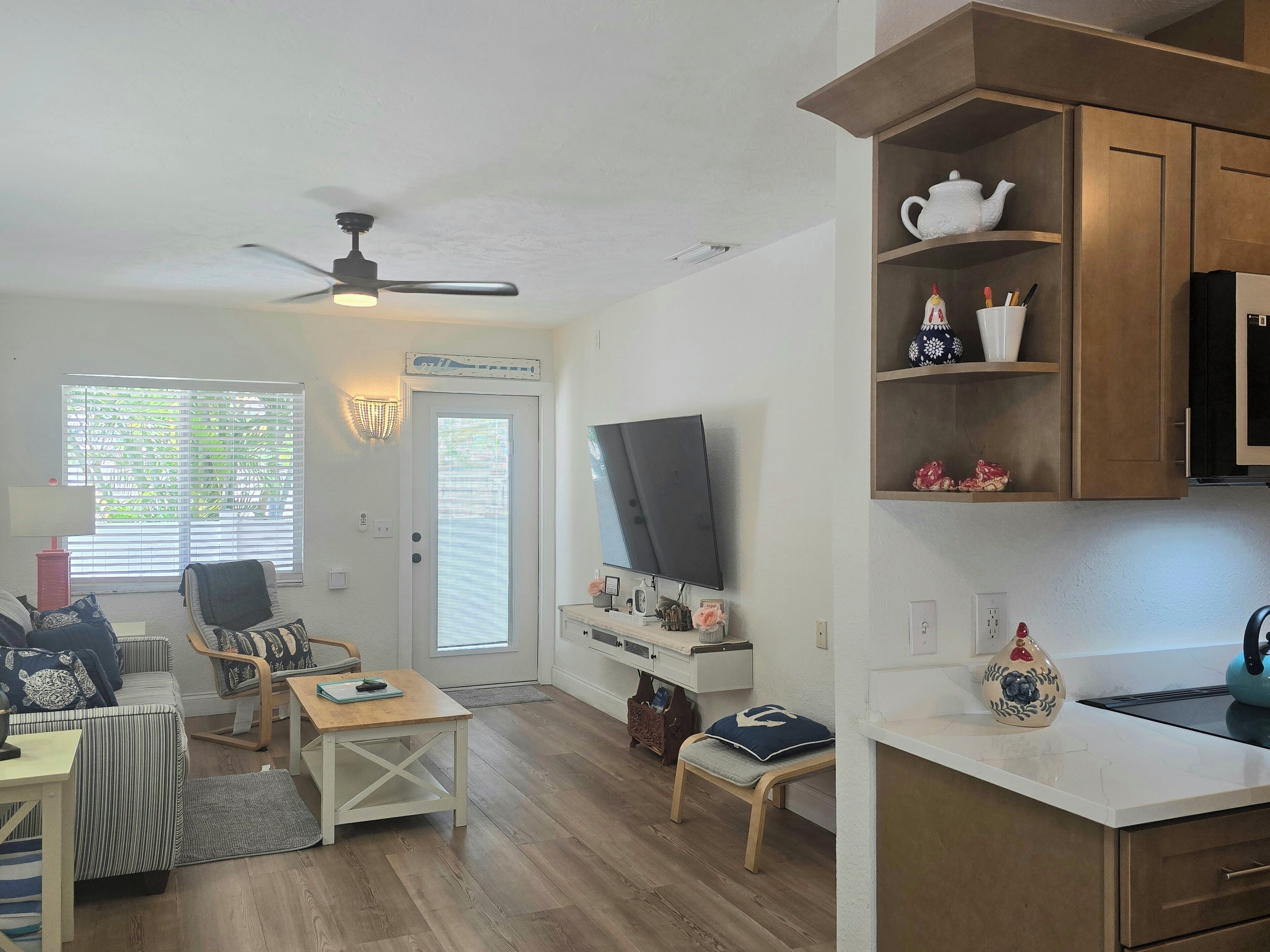 Uma sala de estar com televisão, ventilador de teto e área de refeições com mesa e cadeiras.
