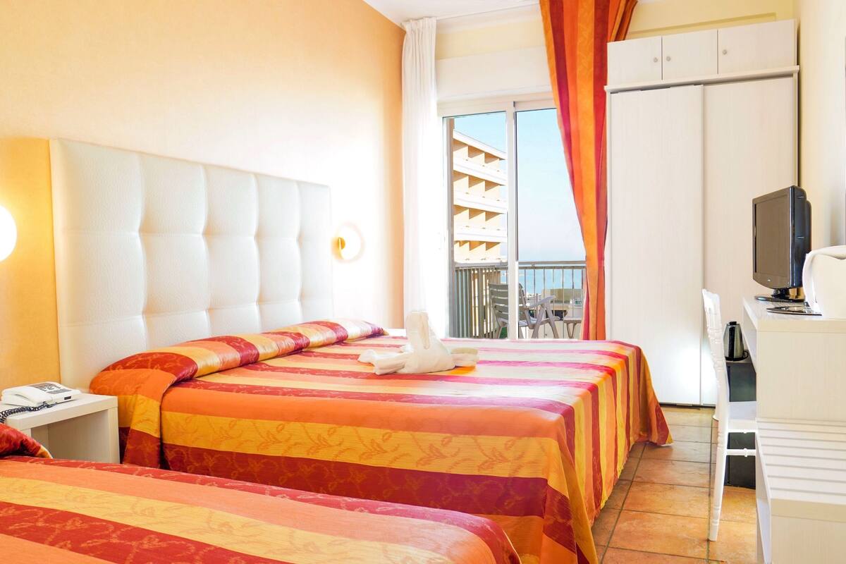 Quarto de hotel com duas camas, uma escrivaninha, televisão e varanda com vista.