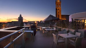 Terraço no telhado com área de estar ao ar livre e vista para uma torre histórica.