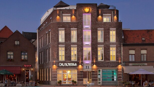 Um hotel com fachada de tijolos, várias janelas e uma placa com a inscrição 'Dux Hotel & Brasserie'.