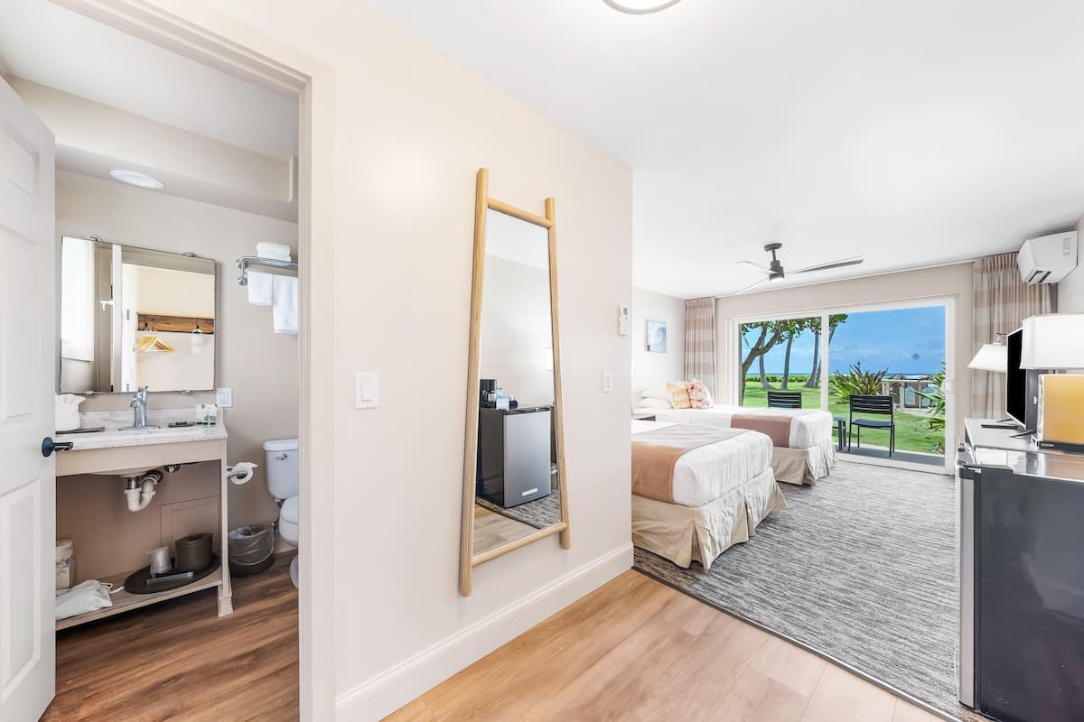 Quarto de hotel moderno com banheiro, um espelho grande, uma cama, uma mesa de trabalho e vista para o exterior.