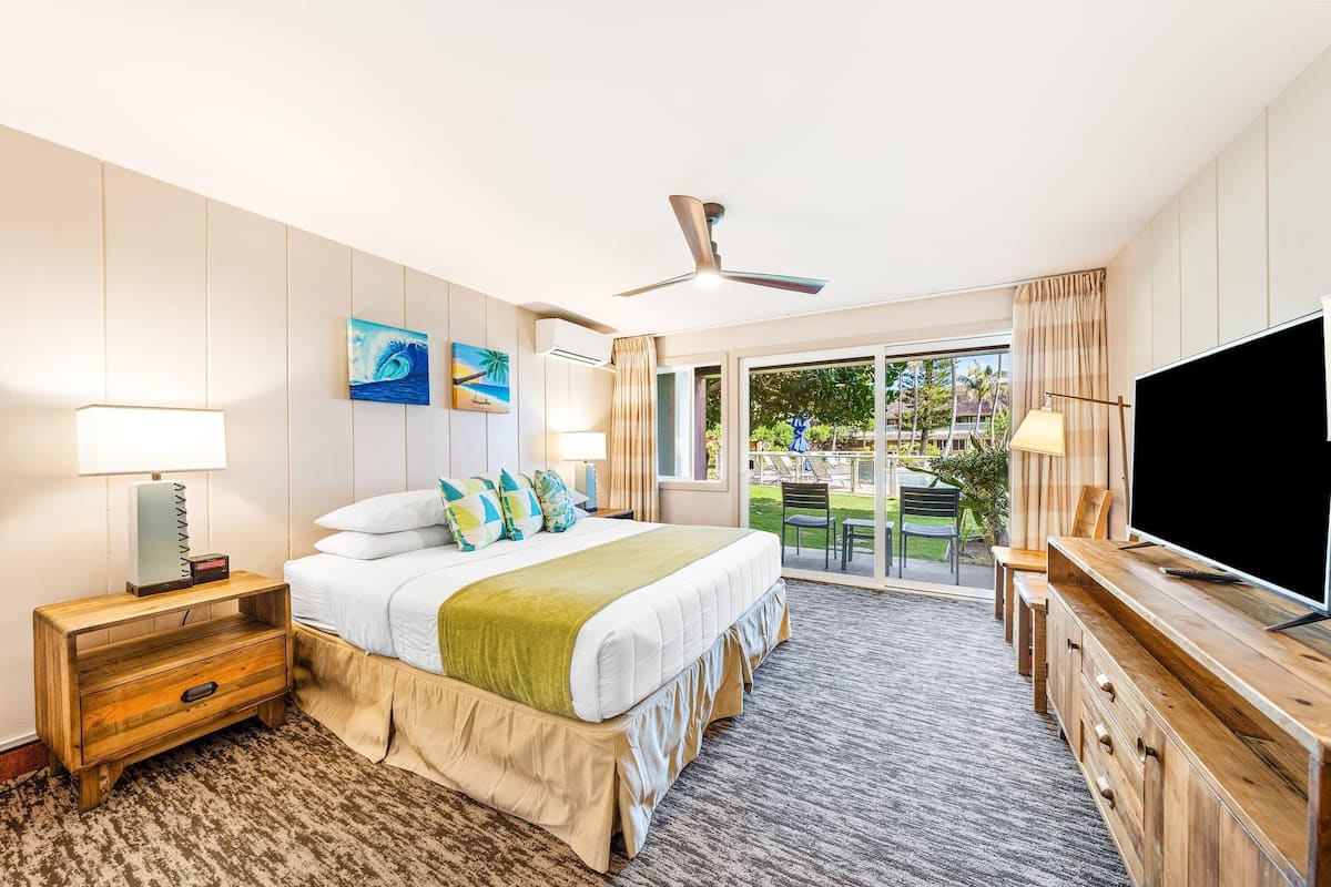 Quarto de hotel com cama, televisão, ventoinha no teto e vista para o exterior.