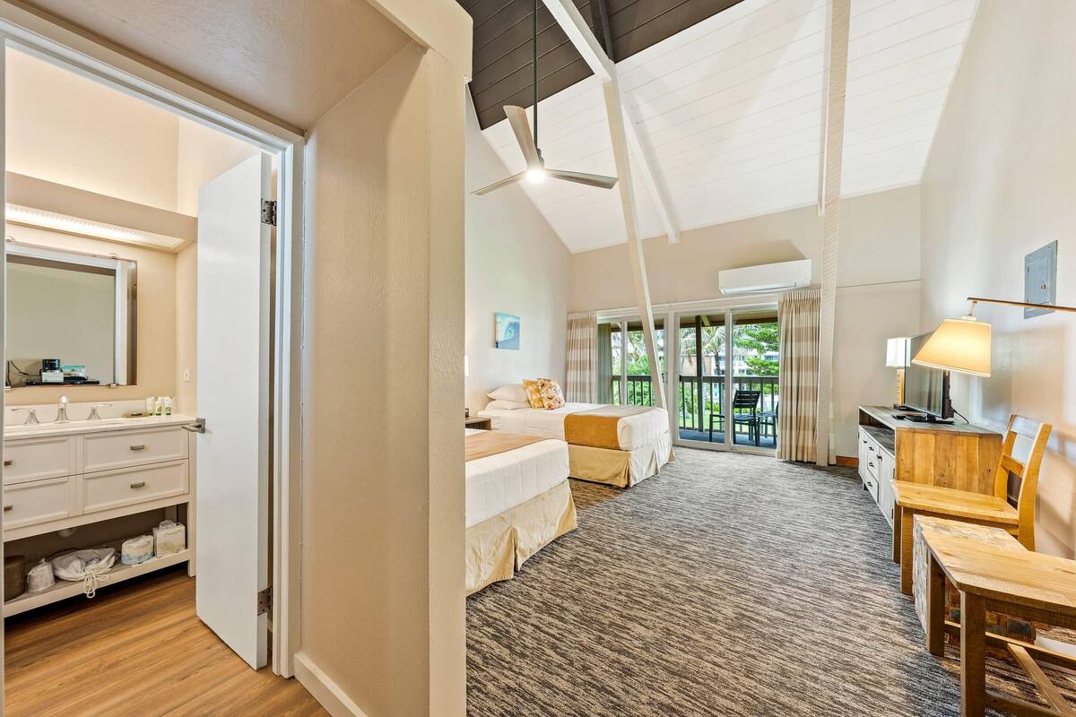 Quarto de hotel com uma cama grande, uma escrivaninha, uma cadeira, um espelho e vista para o exterior.