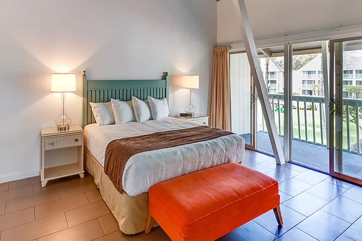 Quarto com cama, mesas de cabeceira, um banco e varanda com vista.