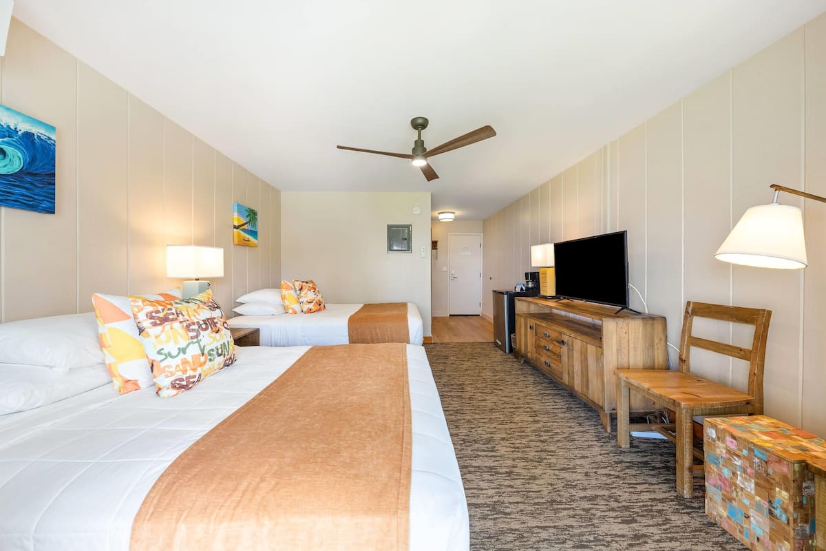 Quarto de hotel com duas camas, televisão, escrivaninha e ventoinha no teto.
