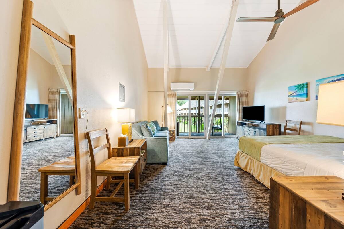 Quarto de hotel com uma cama grande, uma escrivaninha, uma cadeira, uma televisão e uma janela com vista para o exterior.