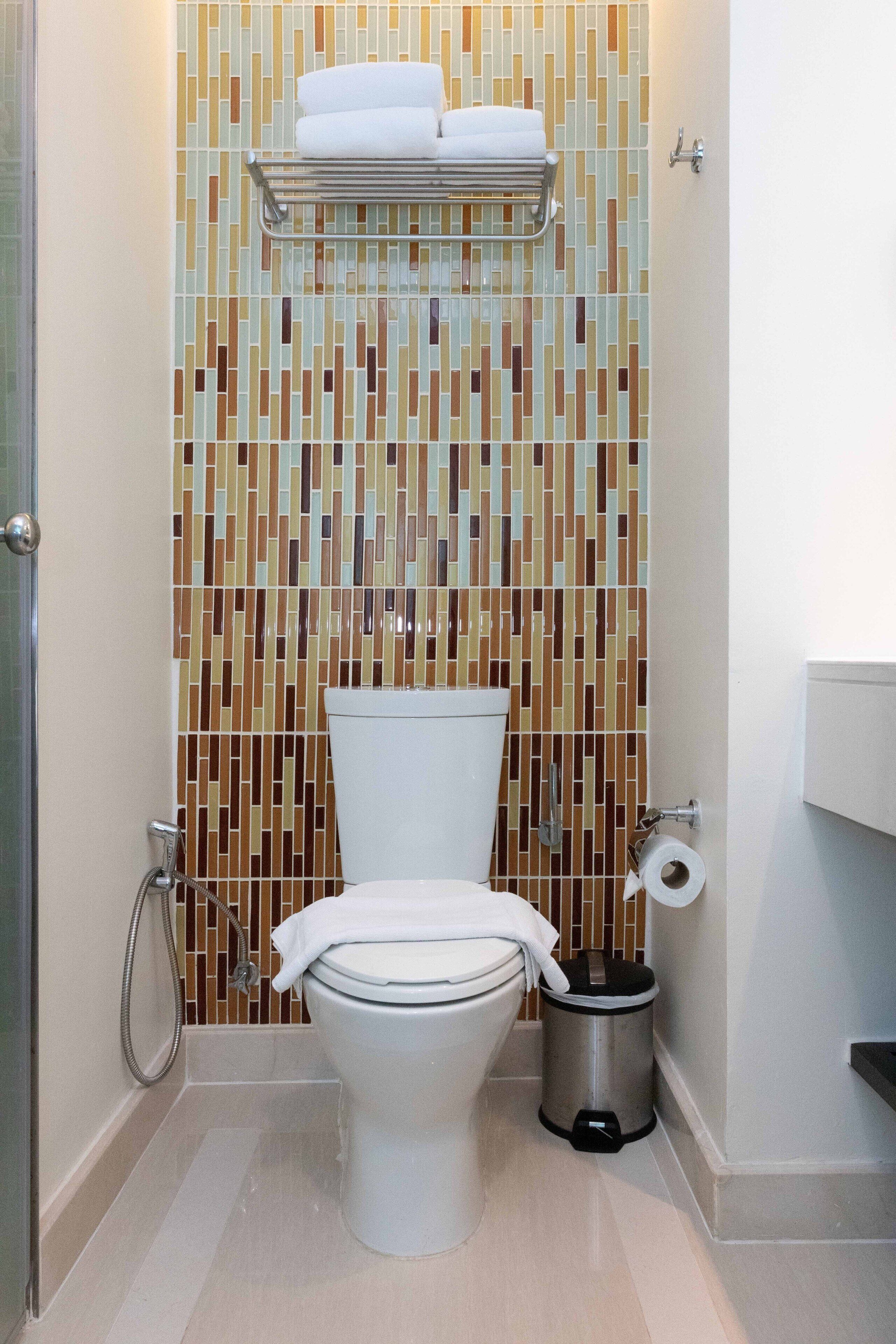 Uma casa de banho moderna com painel de azulejos mosaicos, uma sanita, um contentor de lixo e um porta-toalhas.