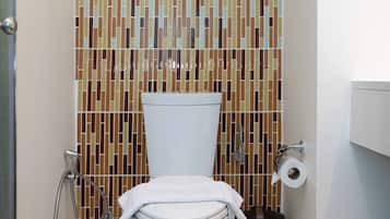Uma casa de banho moderna com painel de azulejos mosaicos, uma sanita, um contentor de lixo e um porta-toalhas.