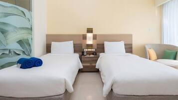 Quarto de hotel com duas camas, uma mesa de cabeceira, uma luminária na parede e uma janela grande com cortinas.