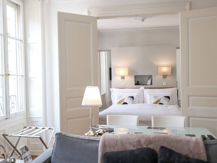 Quarto de hotel com cama, luminárias de cabeceira, escrivaninha e uma cadeira.