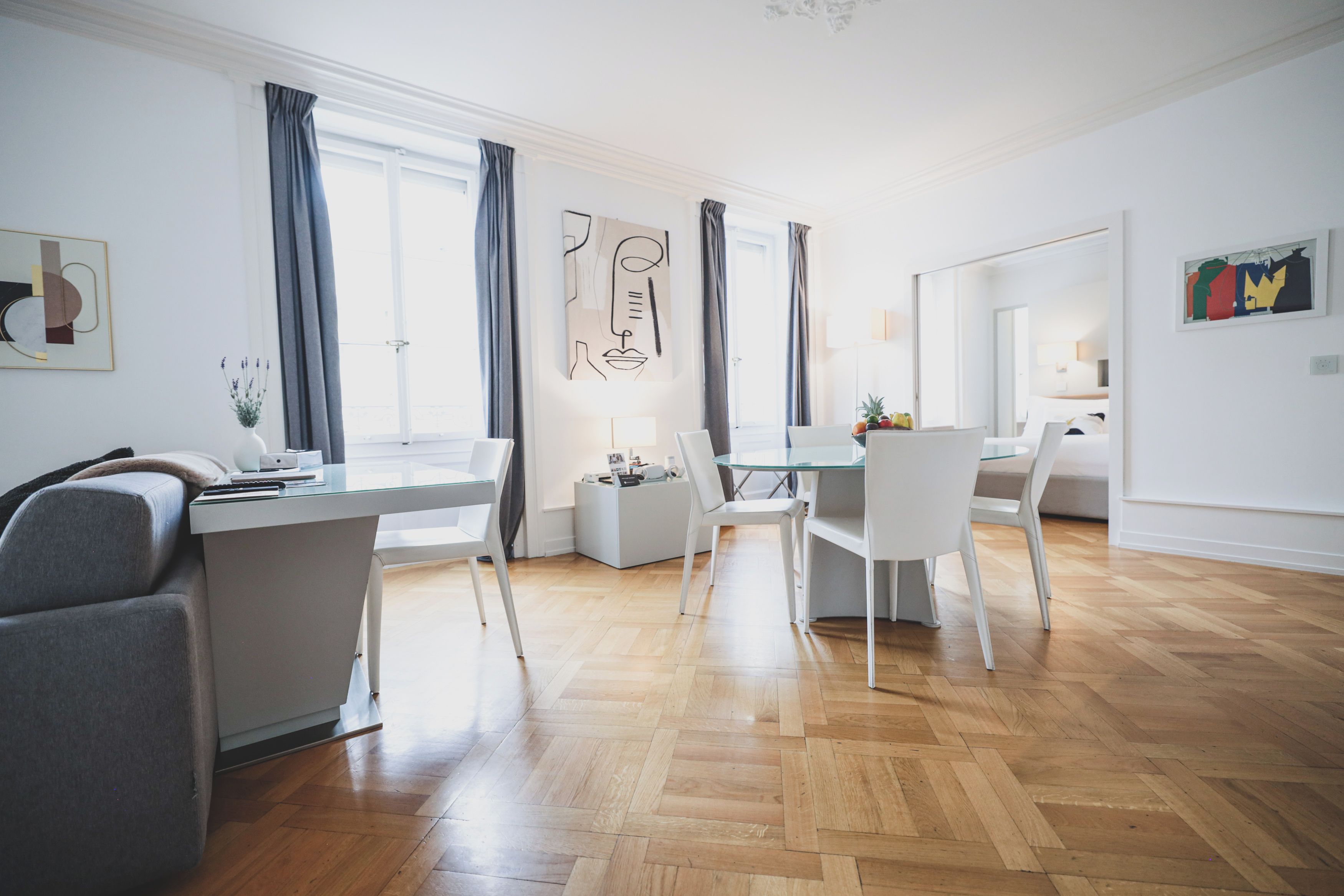 Quarto de hotel moderno com área de refeições, uma janela grande com cortinas e obras de arte nas paredes.