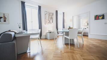 Quarto de hotel moderno com área de refeições, uma janela grande com cortinas e obras de arte nas paredes.