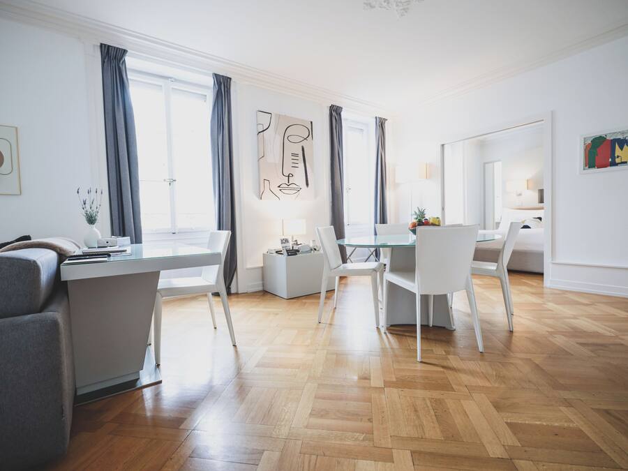 Quarto de hotel moderno com área de refeições, uma janela grande com cortinas e obras de arte nas paredes.