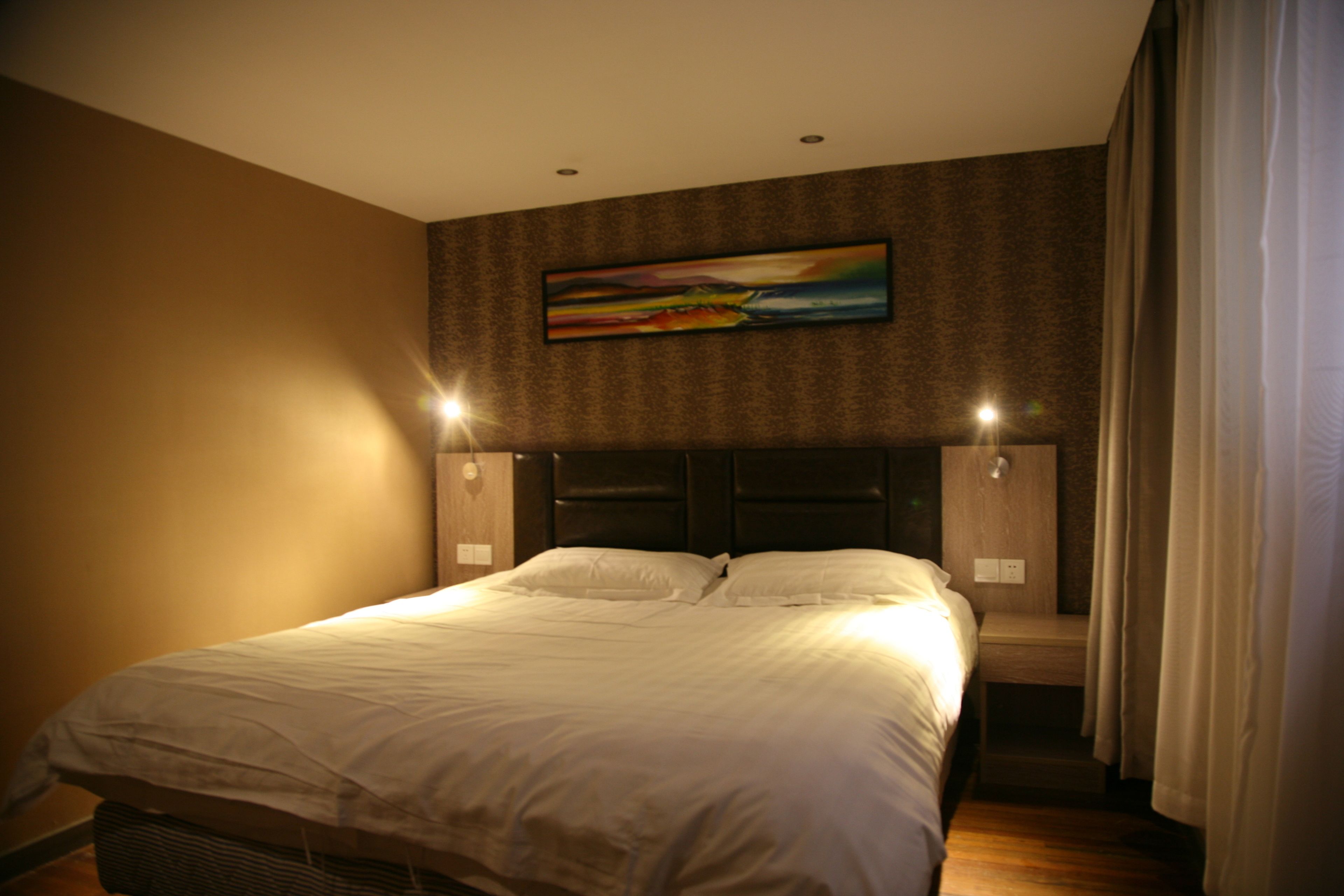 Cama bem arrumada com cabeceira, duas luminárias de cabeceira e um quadro acima da cama.