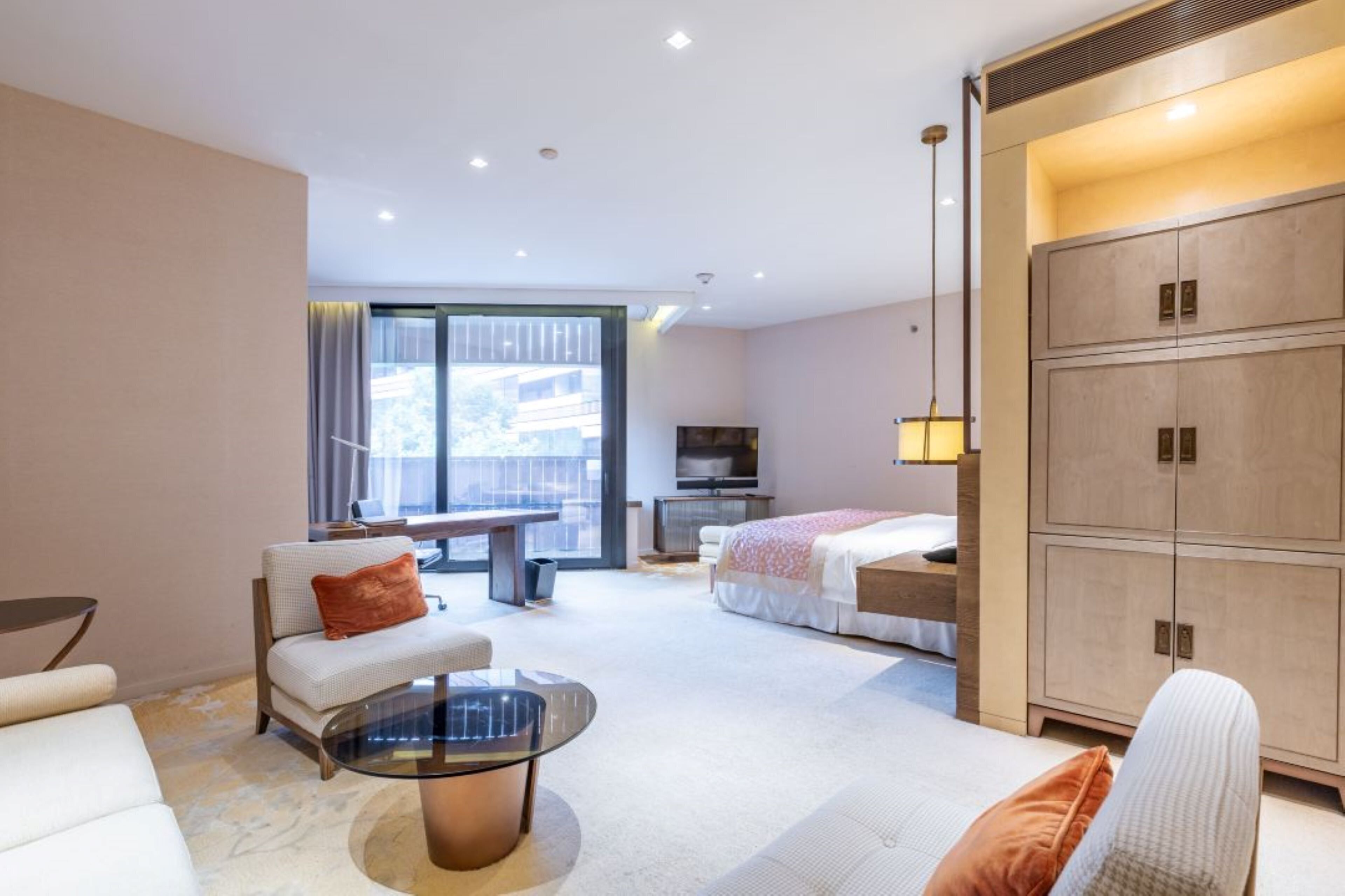 Quarto de hotel moderno com sofá, mesa de centro de vidro, cama com cabeceira, guarda-roupa e televisão.