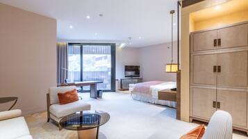 Quarto de hotel moderno com sofá, mesa de centro de vidro, cama com cabeceira, guarda-roupa e televisão.