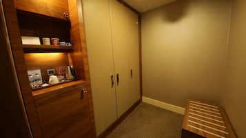 Quarto de hotel com guarda-roupa de madeira, um pequeno espaço com produtos de higiene e um banco de madeira.