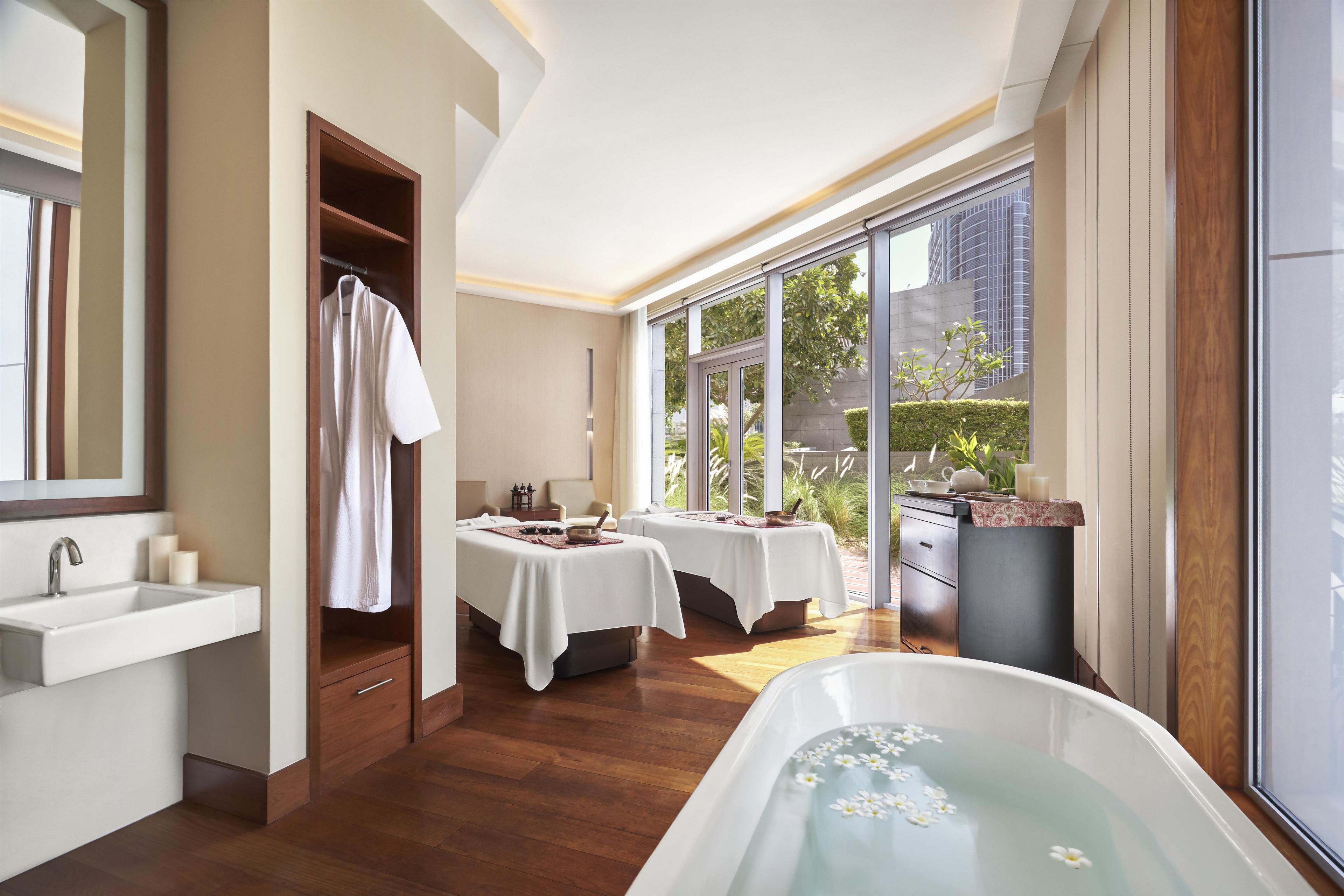 Um banheiro moderno com banheira, duas mesas de massagem, um lavatório e uma janela grande que oferece vista para o exterior.