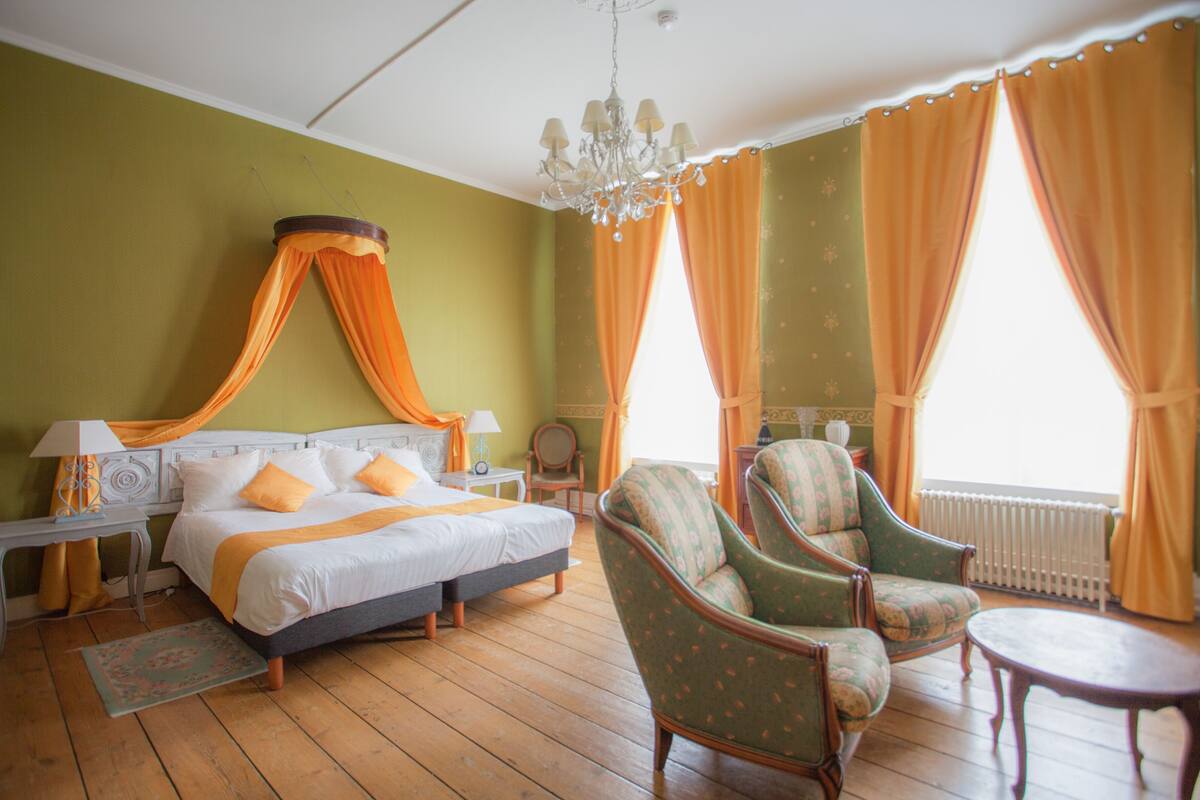 Quarto com cama, duas cadeiras, uma mesa, abajur e lustre.