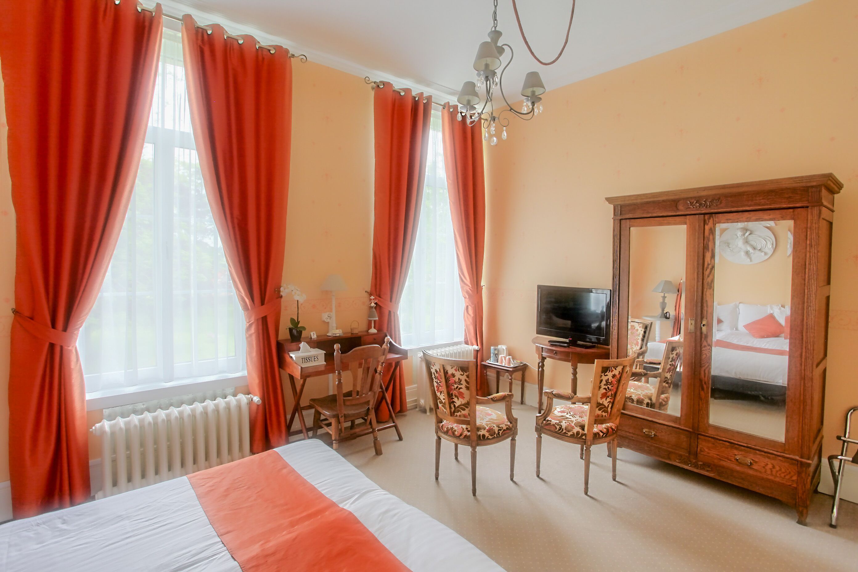 Quarto de hotel com cama, escrivaninha, cadeira, televisão e guarda-roupa.