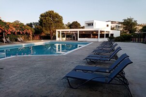 Piscina com espreguiçadeiras e um edifício moderno ao fundo.
