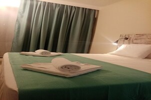 Quarto de hotel com cama, colcha verde, travesseiros brancos e cabeceira.