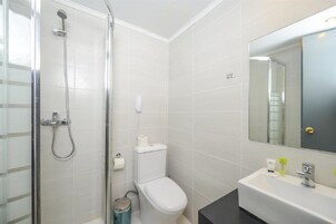 Uma casa de banho moderna com chuveiro em cabine de vidro, sanita branca e lavatório com artigos de higiene pessoal.