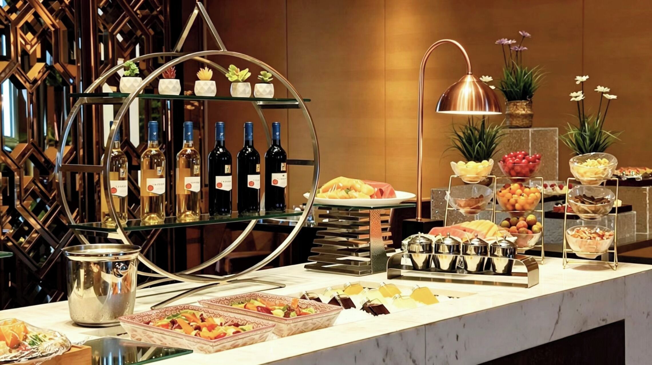 Disposição de buffet com diversos alimentos, seleção de vinhos e plantas decorativas.