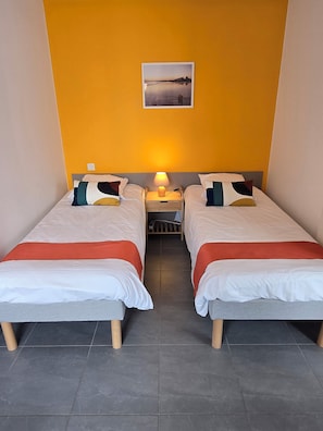 Quarto de hotel com duas camas, mesa de cabeceira com abajur e um quadro na parede.