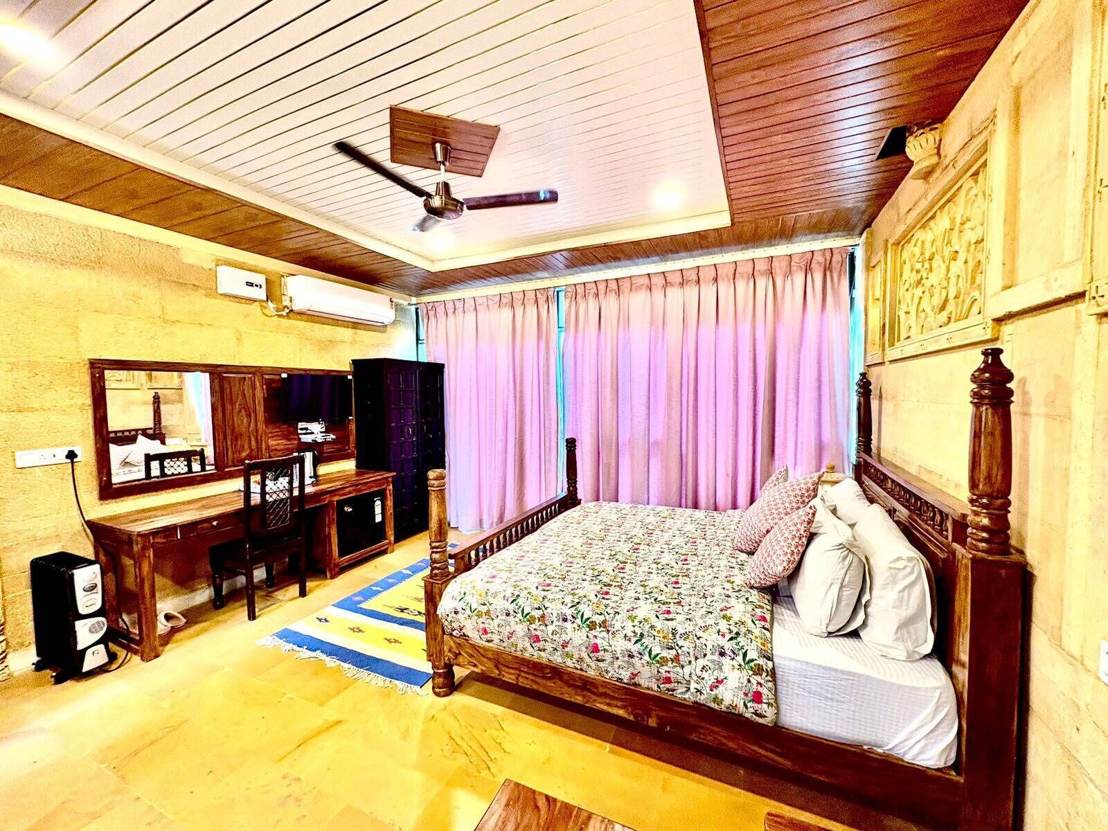Quarto com cama, escrivaninha, cadeira, televisão e ventilador de teto.