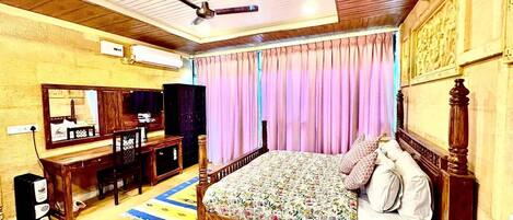 Quarto com cama, escrivaninha, cadeira, televisão e ventilador de teto.