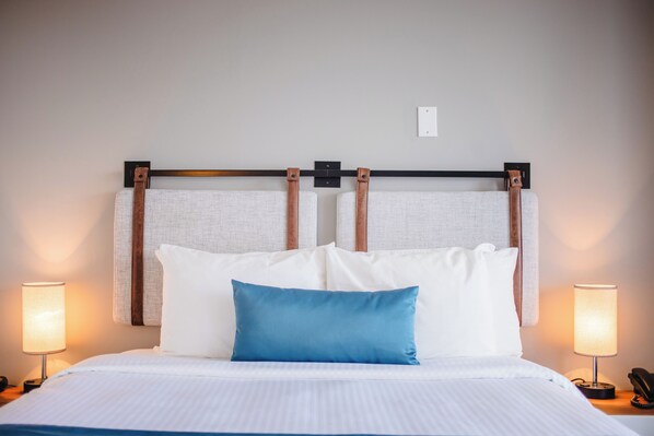 Uma cama bem arrumada com roupa de cama branca e azul, cabeceira de madeira e duas luminárias de cabeceira.