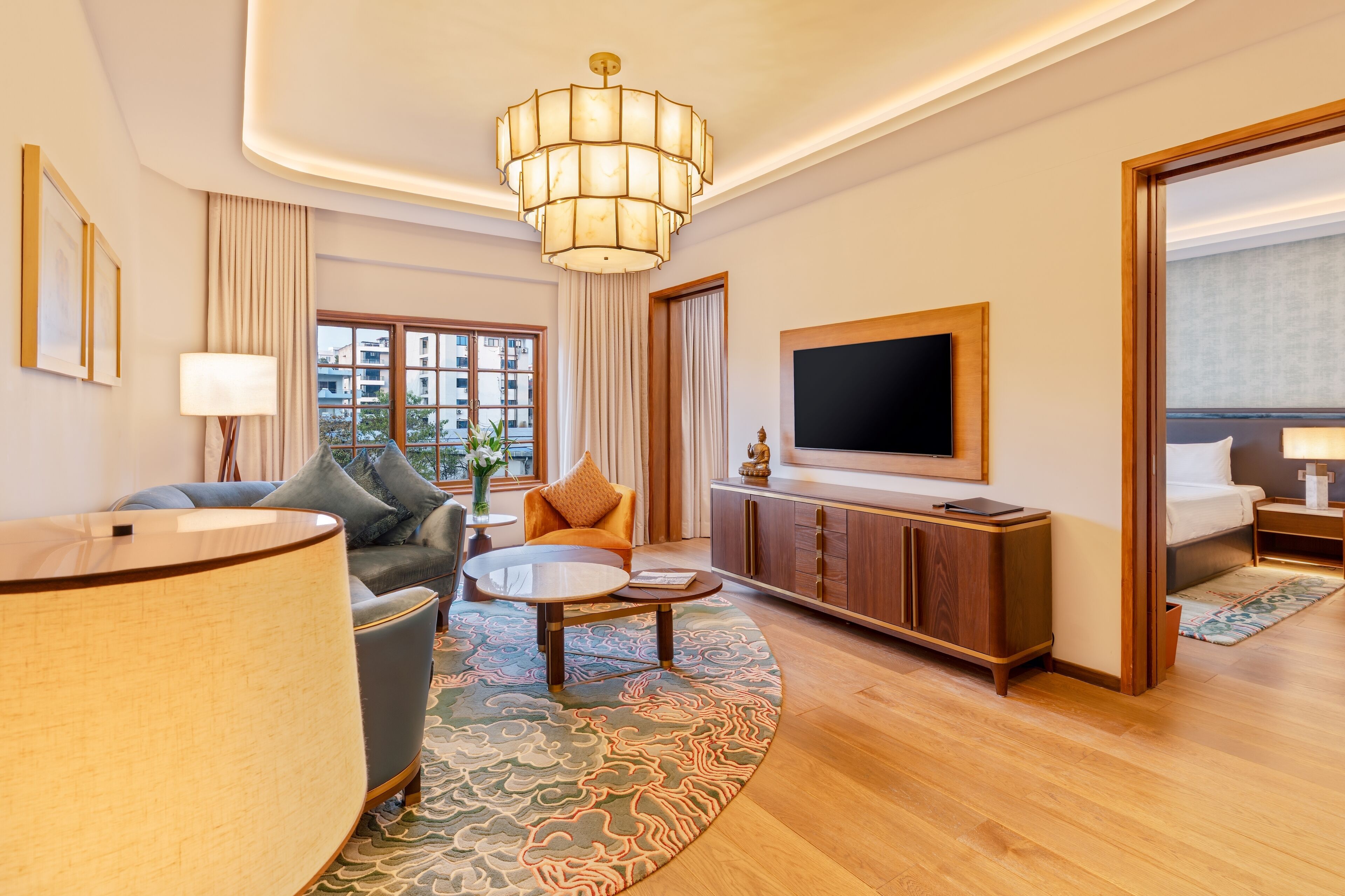 Quarto de hotel com sofá, poltrona, mesa de centro, televisão e uma janela grande.