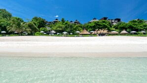 Um resort à beira-mar com bangalôs sobre a água, águas turquesas cristalinas e vegetação exuberante.