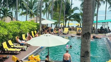 Área de piscina com espreguiçadeiras e guarda-sóis, cercada por palmeiras.