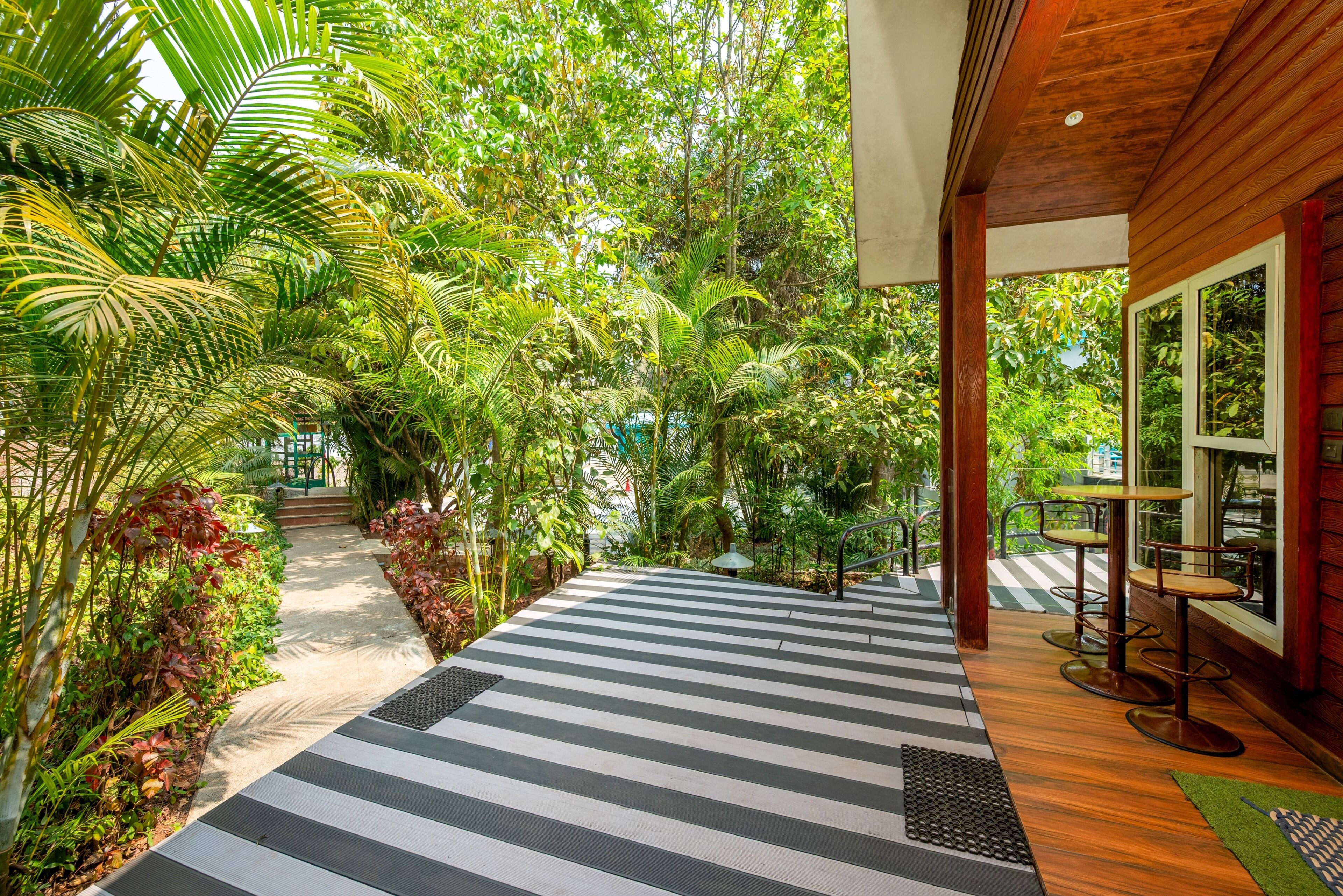 Caminho em um jardim tropical que leva a uma construção de madeira com banquetas.