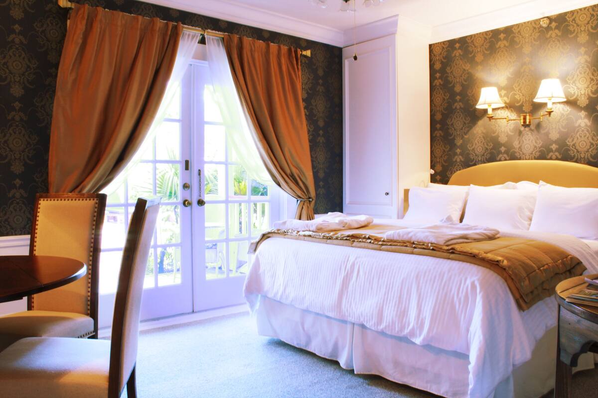 Quarto de hotel com cama, uma cadeira, uma mesa e porta que dá para uma varanda.