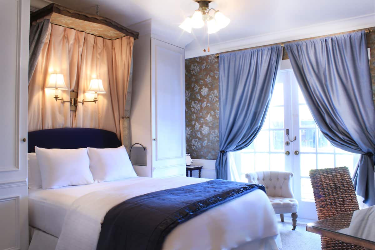 Quarto de hotel com uma cama grande, duas luminárias de cabeceira, uma cadeira e vista para o exterior.