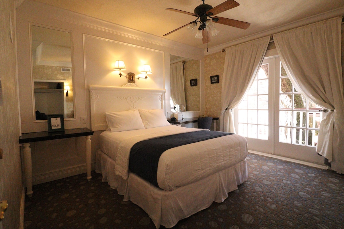 Quarto de hotel com cama grande, ventoinha no teto, espelho e janela com cortinas.