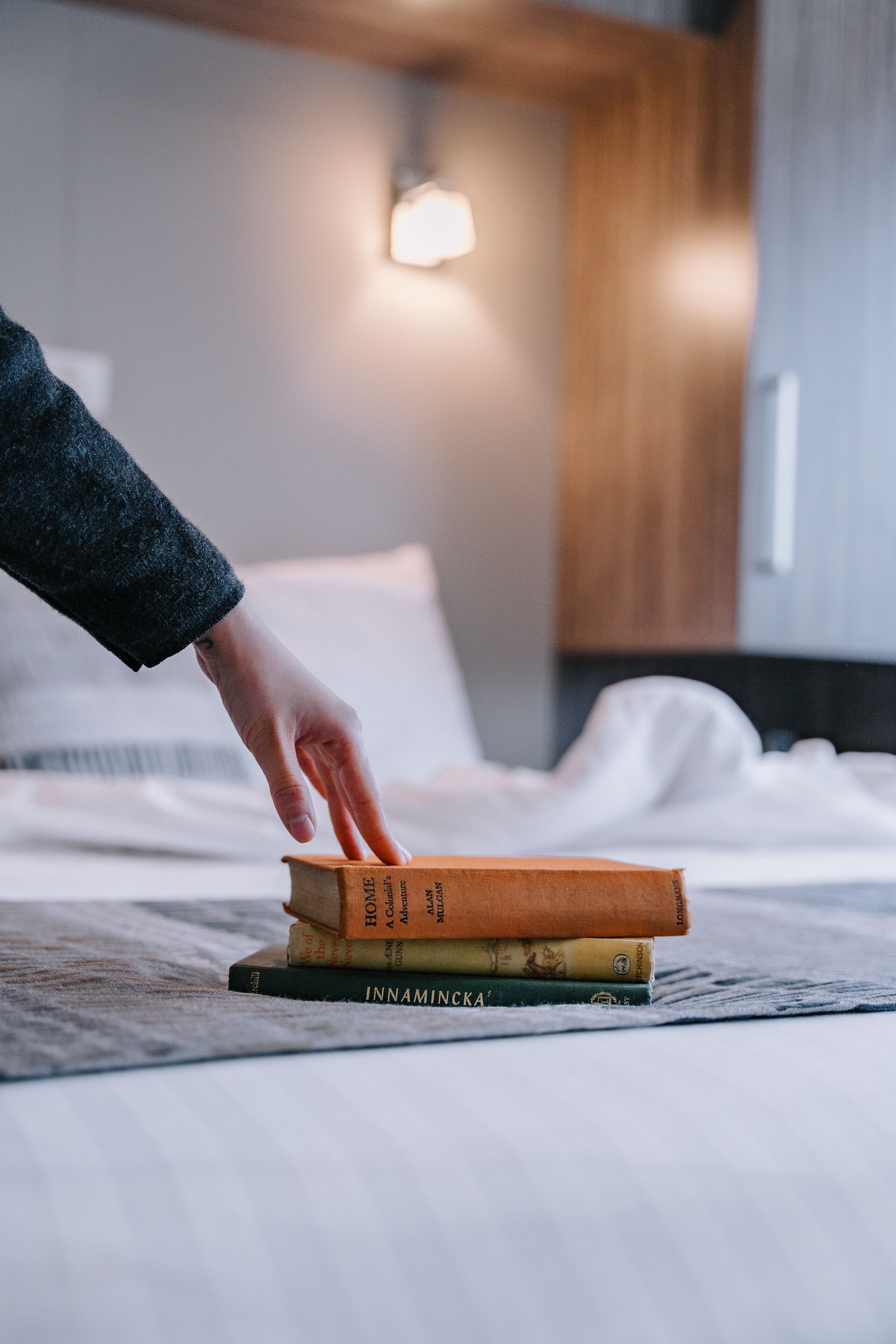 Uma mão colocando um livro sobre uma pilha de livros em uma cama.