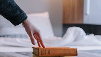 Uma mão colocando um livro sobre uma pilha de livros em uma cama.