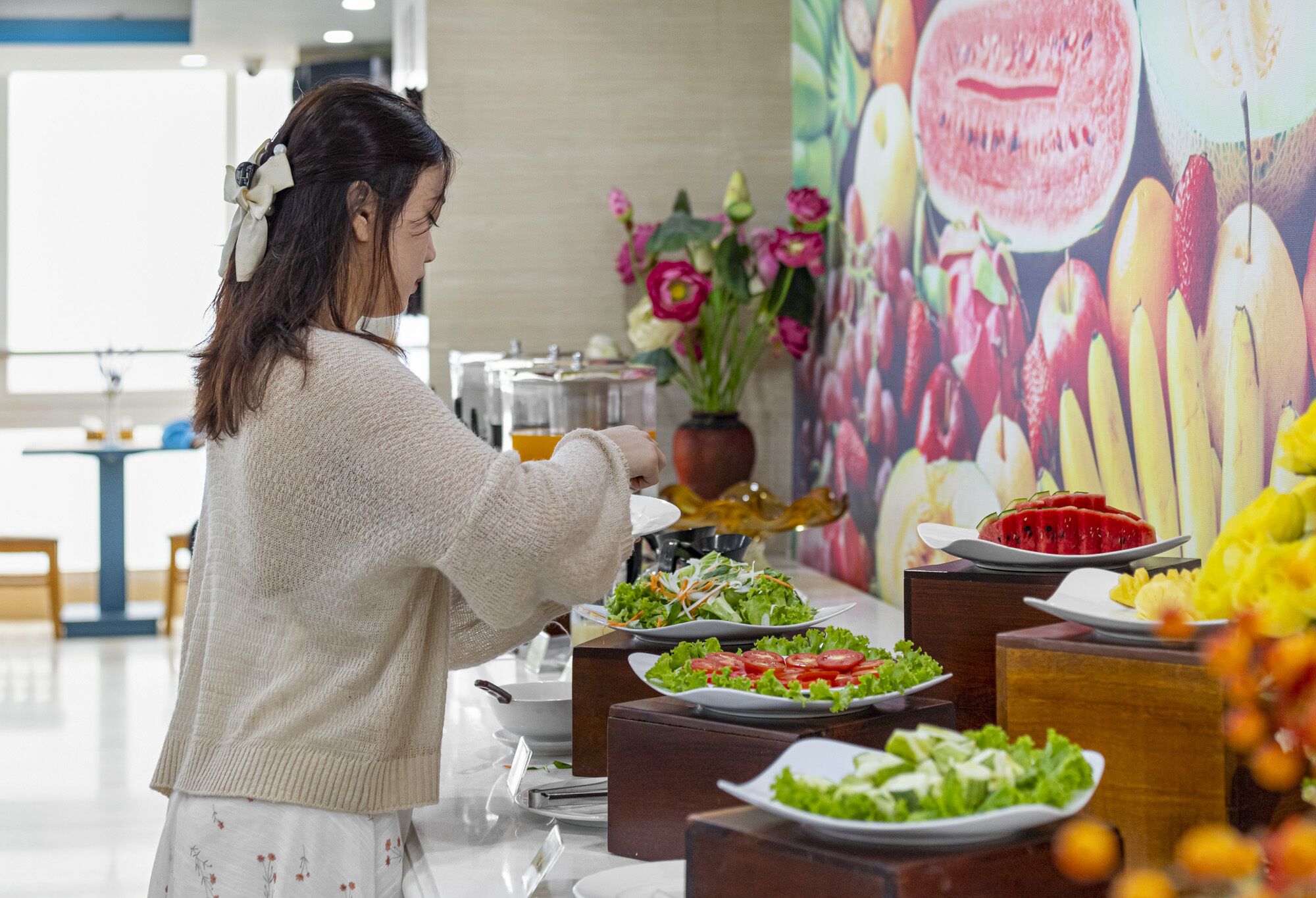 Disposição de buffet com diversos pratos e um mural grande de frutas ao fundo.