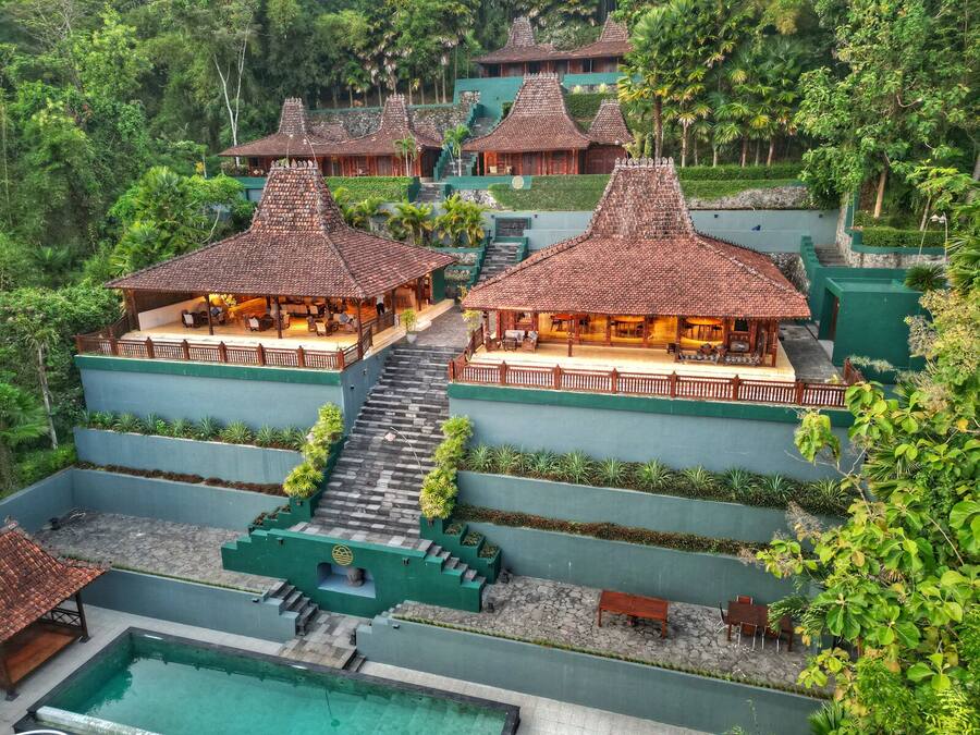 Um resort com vários edifícios tipo bungalow, cada um com telhado em cerâmica e rodeado por vegetação exuberante.