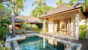 Uma área de piscina com borda de pedra, um espaço coberto para relaxar e um edifício com telhado em cerâmica.
